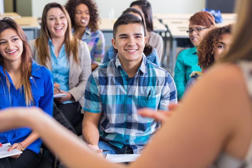 Teens smiling while listening to speaker during presentation in school ...